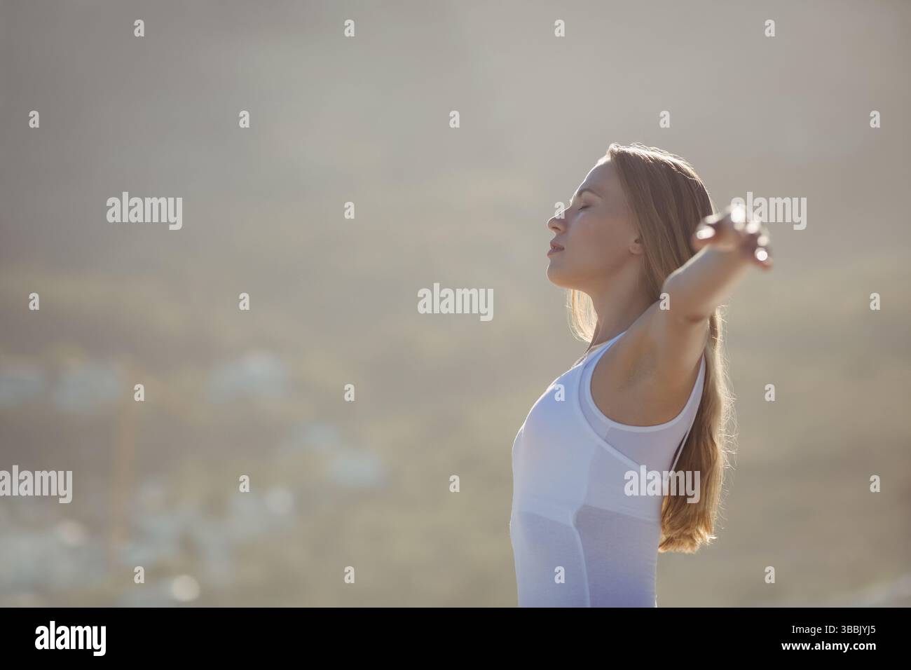Woman is standing arms outstretched on hillside, breathing deeply in ...