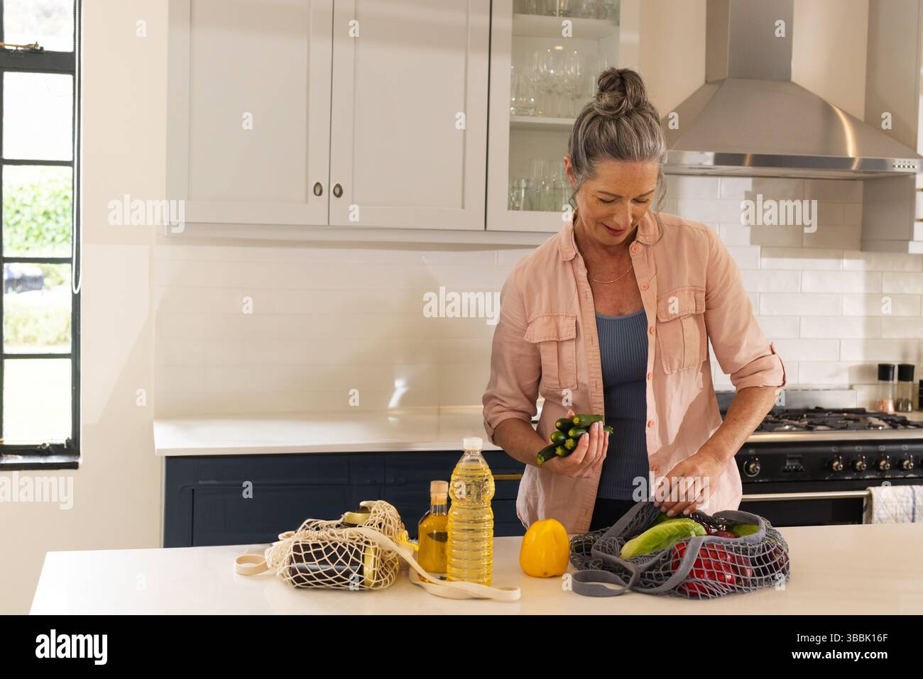 Sorting senior woman arranging vegetables at kitchen island, with mesh ...