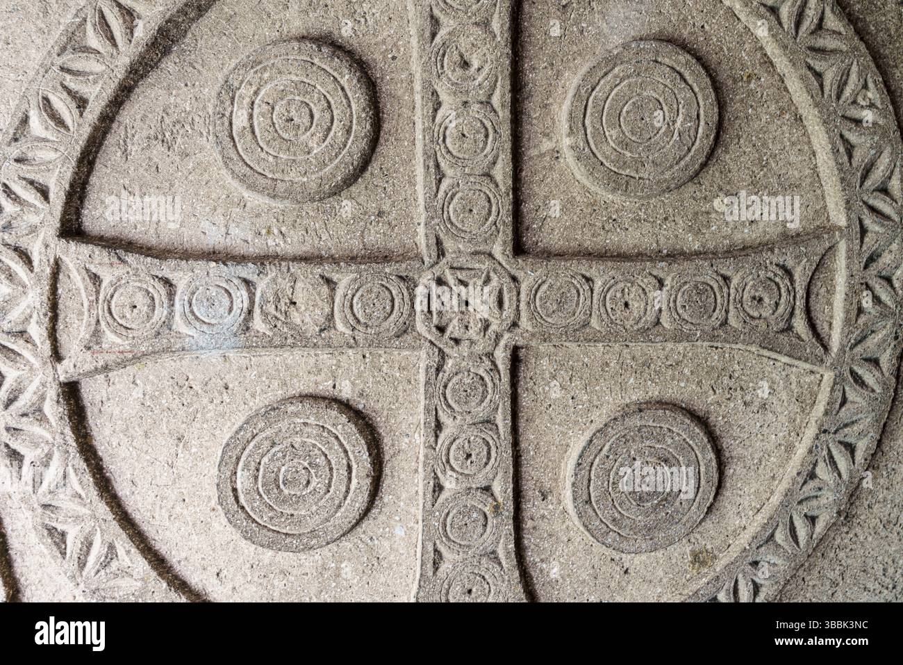 A circular stone relief with geometric patterns and crosses is carved ...