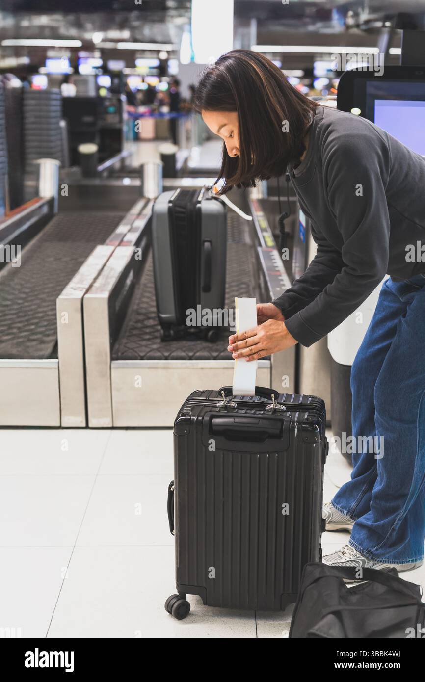 Woman putting flight tag on her luggage at check in counter at airport ...