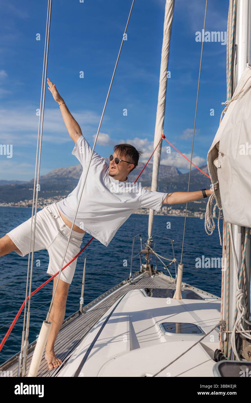 Man balancing on one leg aboard sailboat, arms extended in dynamic pose ...