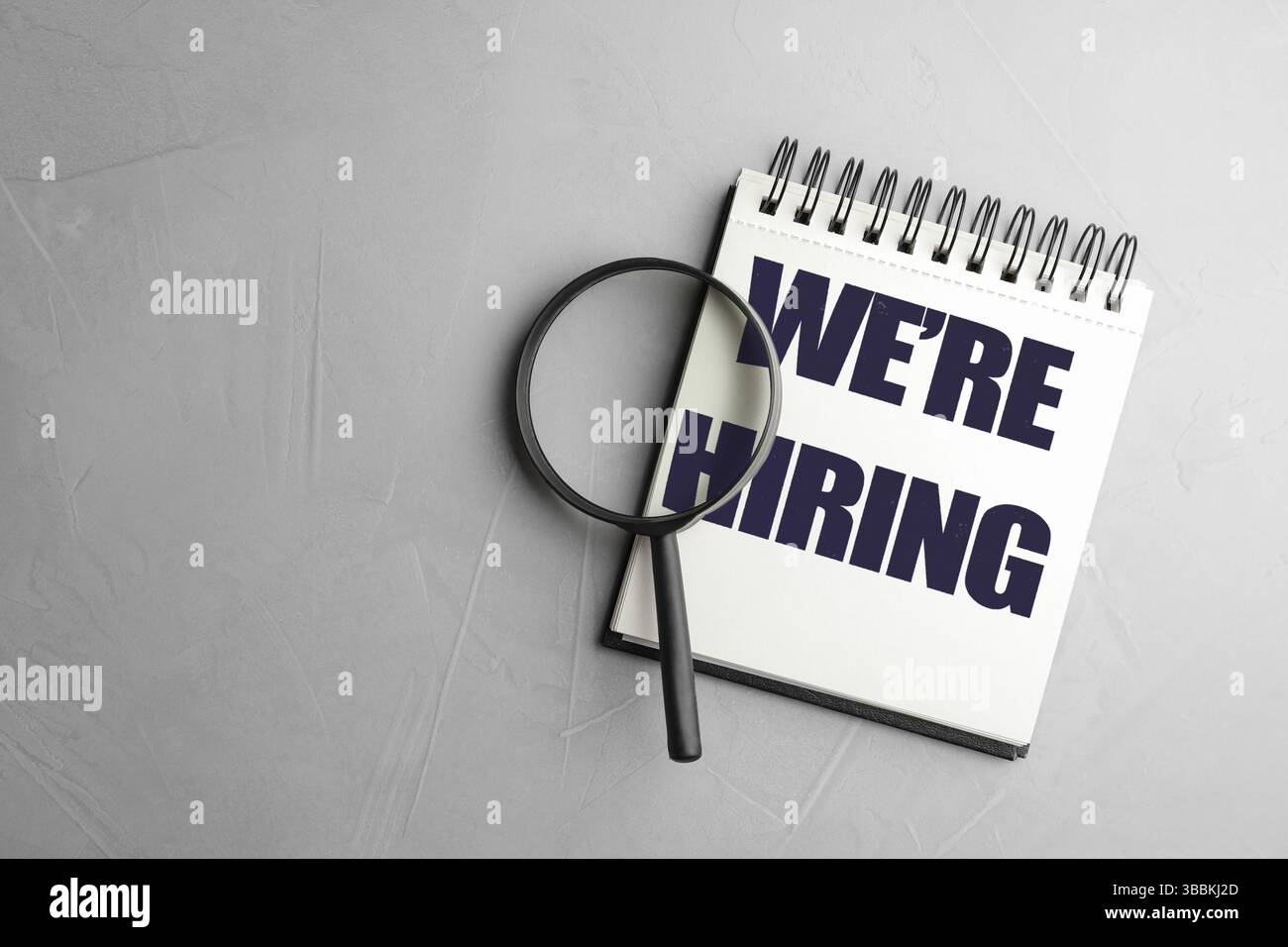 We Are Hiring. Notebook and magnifying glass on grey background, top ...