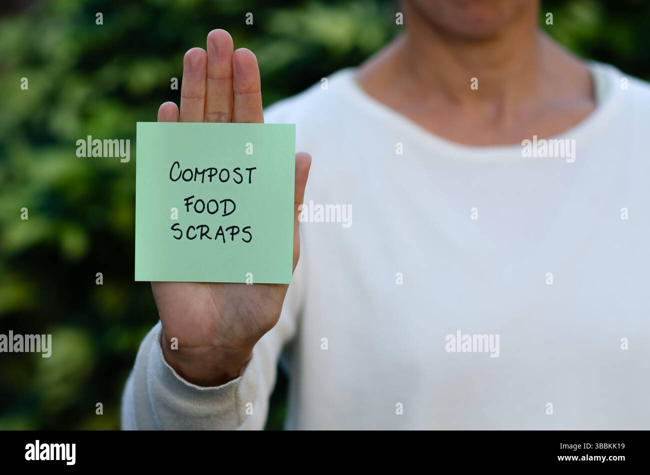 A woman holding a green handwritten sign reminder of composting food ...