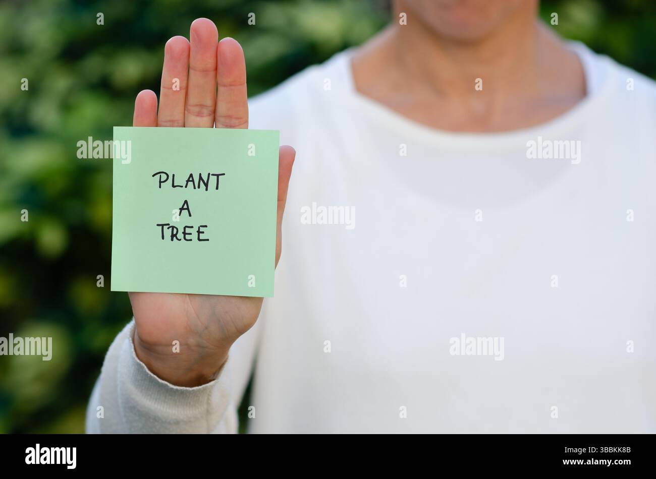 A woman holding a green handwritten sign reminder of planting a tree ...