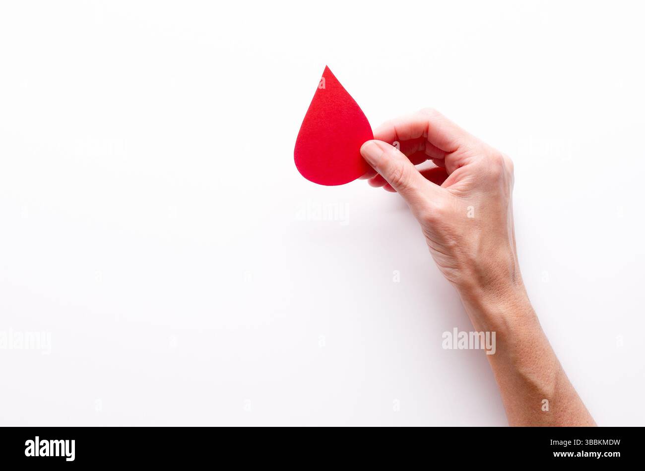 A female hand holding a paper drop of blood on white background and ...