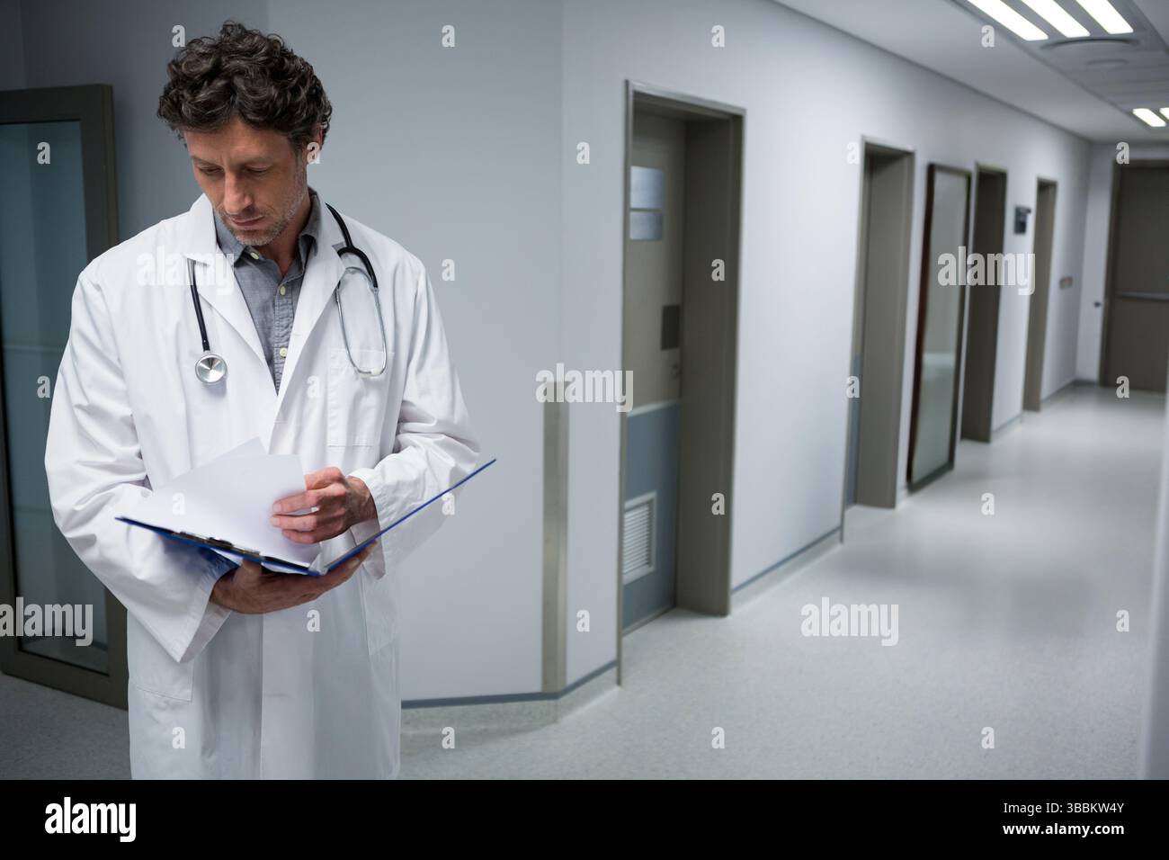 Reading male doctor reviewing chart in hospital hallway, with ...