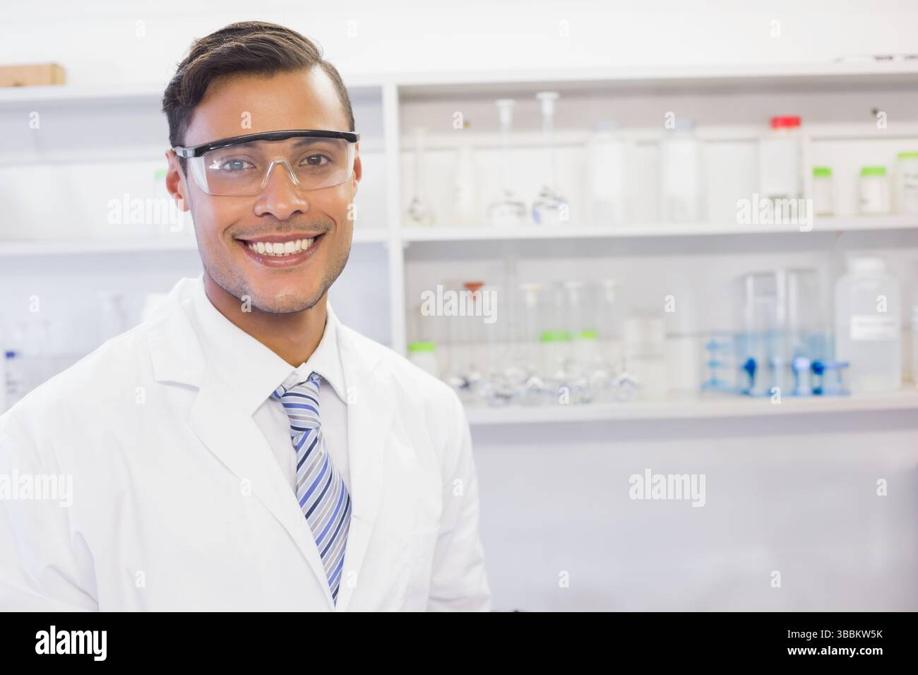 Smiling male scientist wearing lab coat and safety goggles working in ...