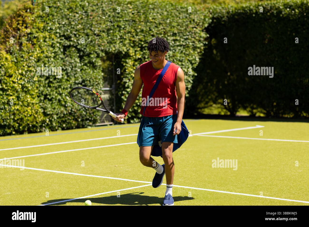 Young man walking on tennis court, carrying racket and blue sports bag ...