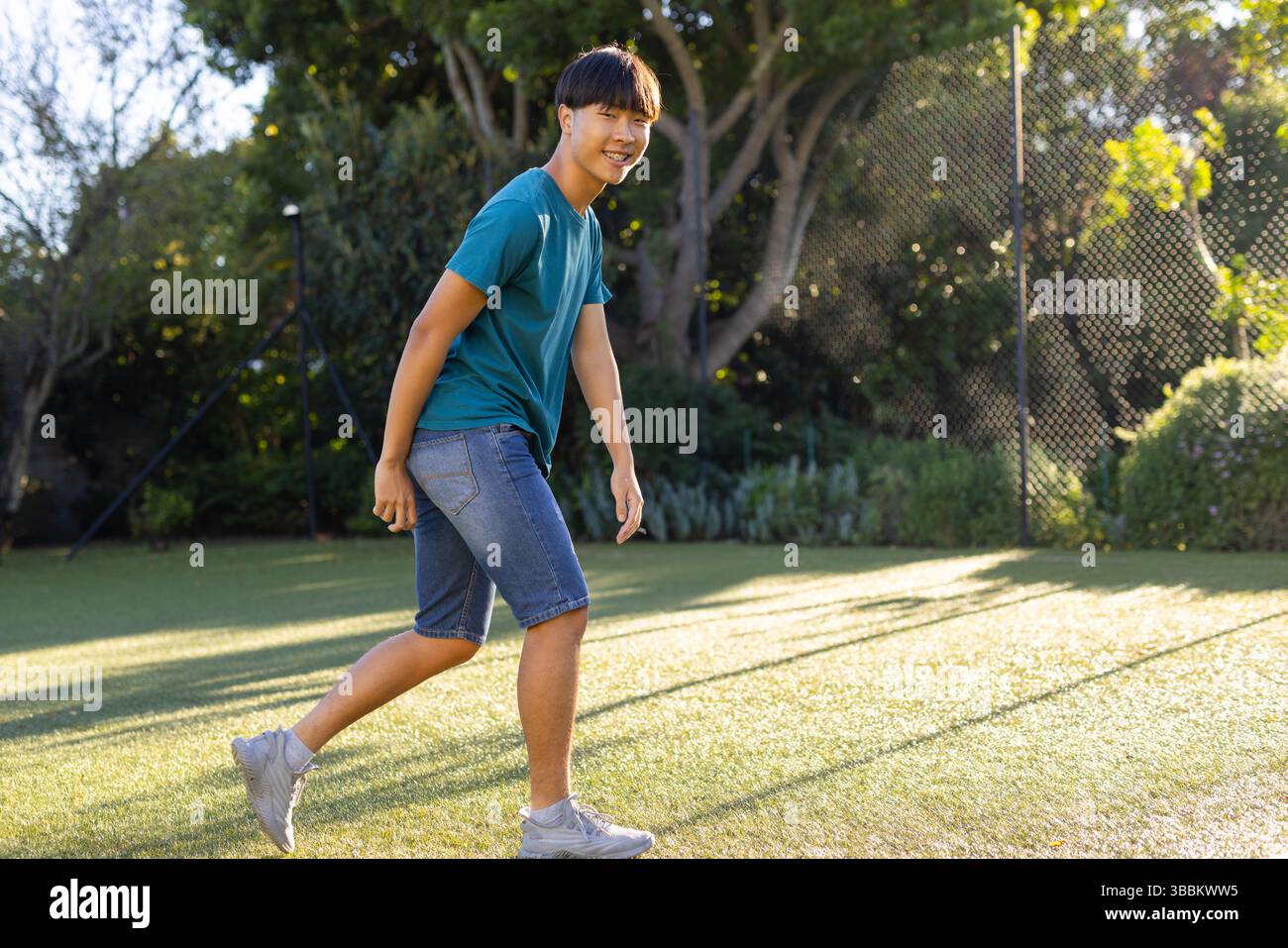 Young Asian man walking across synthetic turf in backyard, with chain ...
