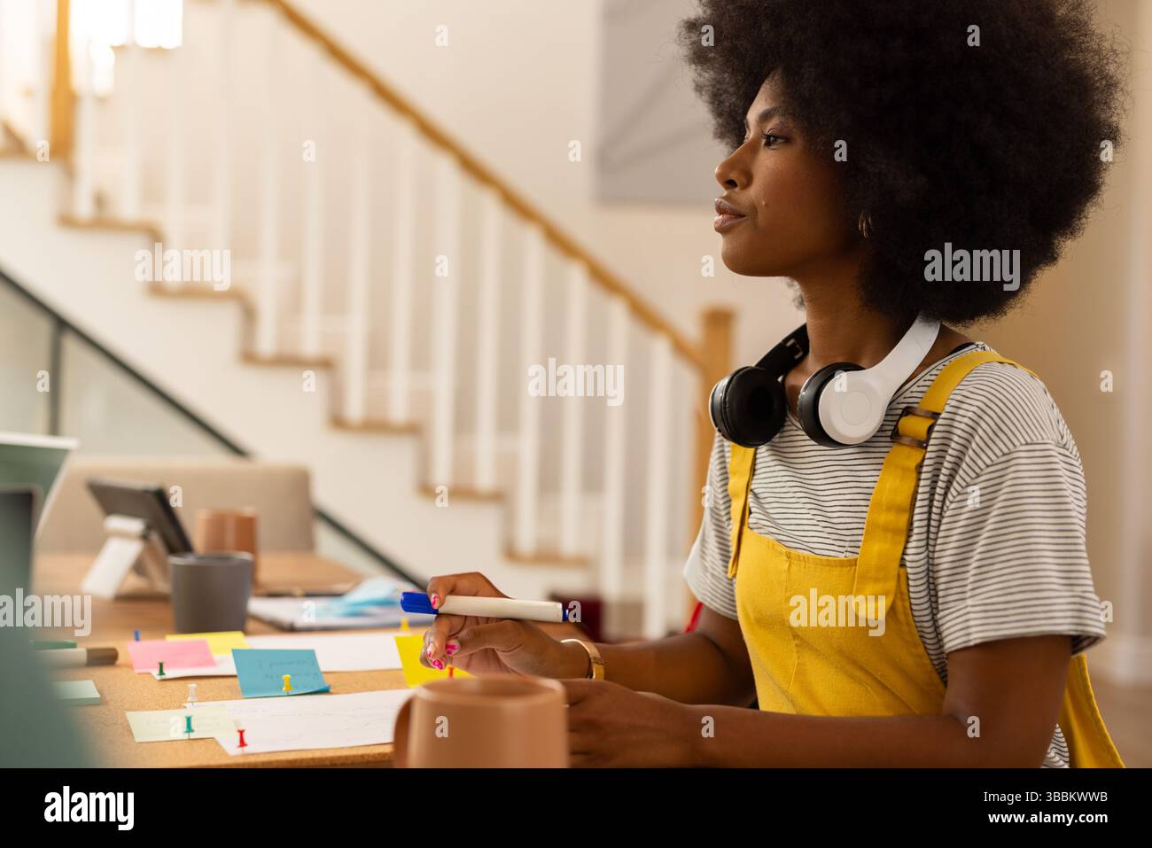 African American woman writing on sticky notes in home workspace, with ...