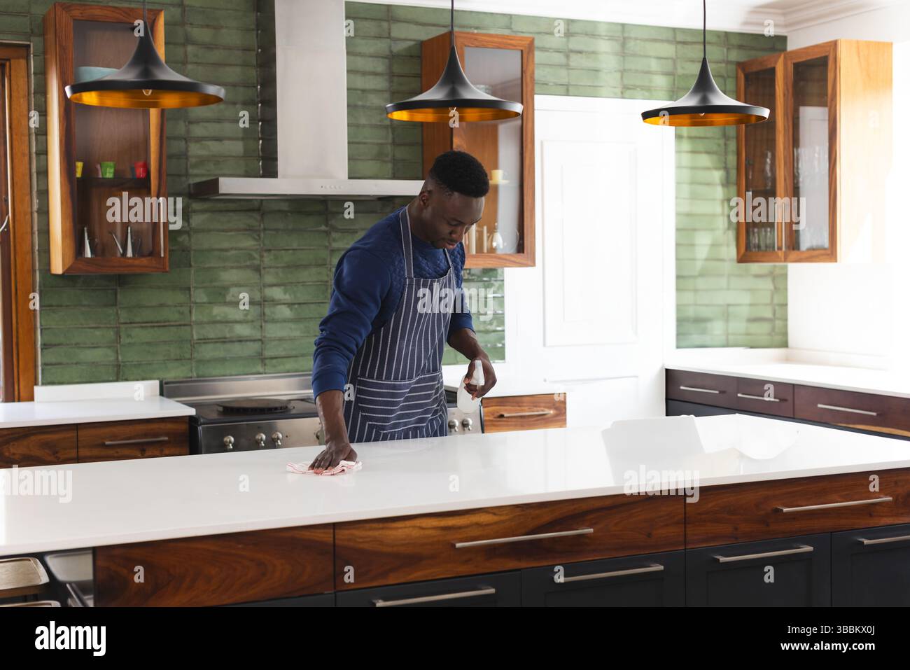 African American man cleaning quartz countertop in modern kitchen, with ...