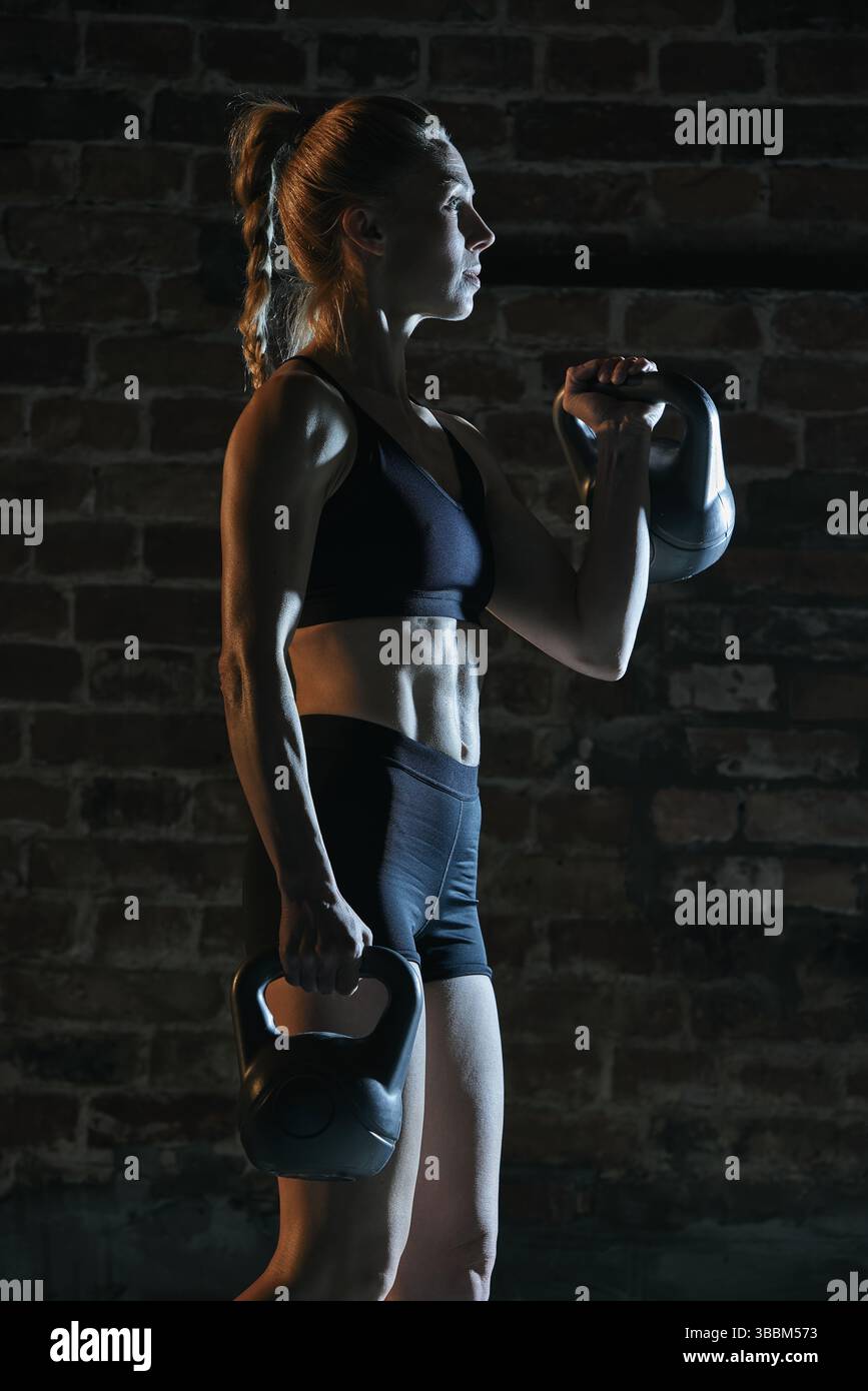 Fit woman holding kettlebells in standing pose during strength training ...