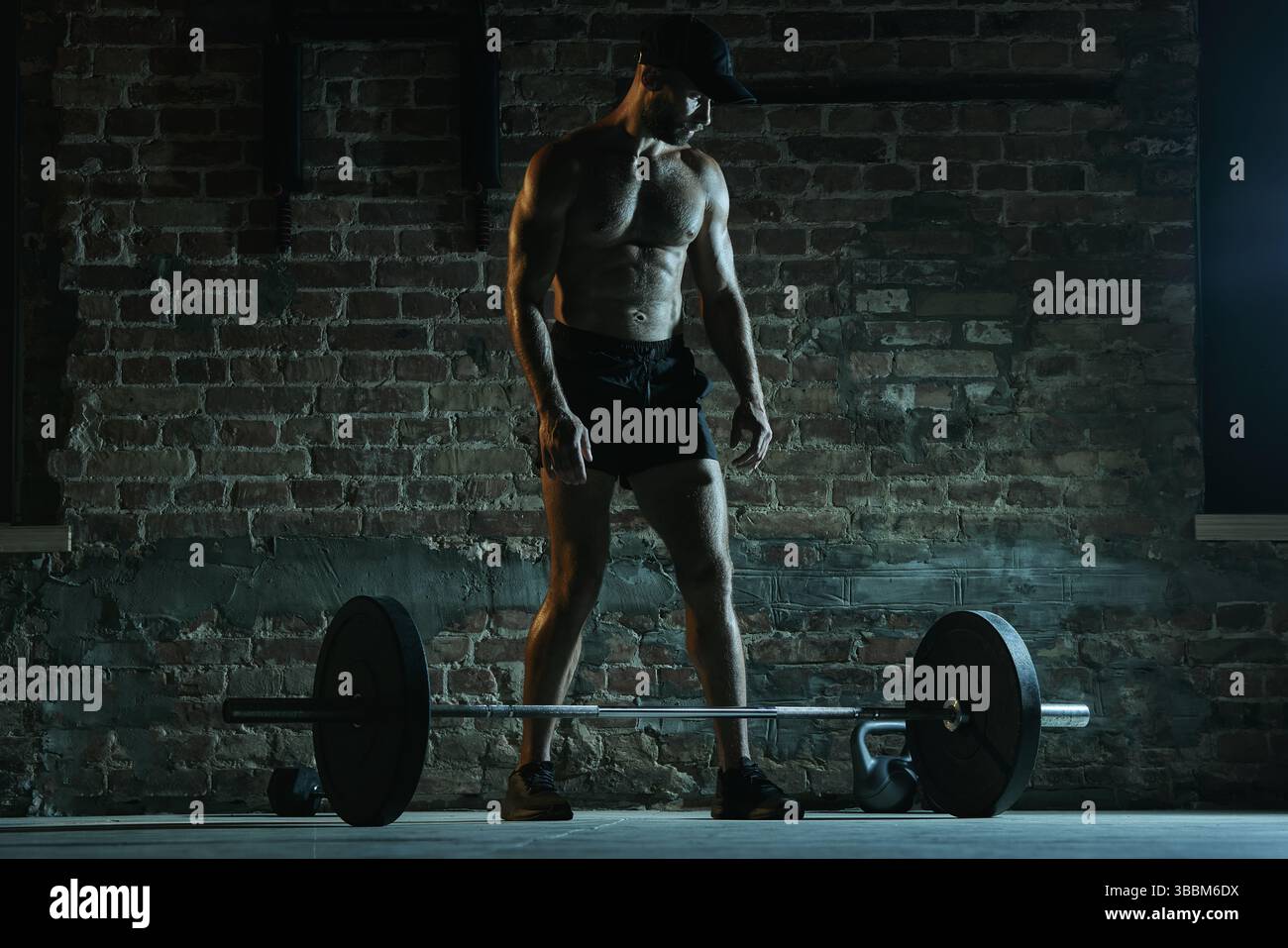 Fit muscular man in spotlight standing behind loaded barbell with tense ...