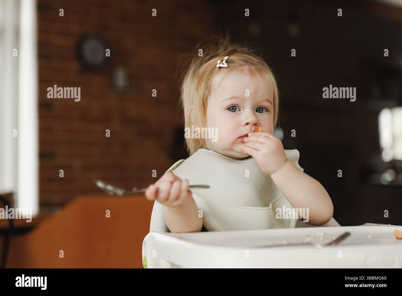 Eleven month infant girl or toddler sitting on high chair with bib ...