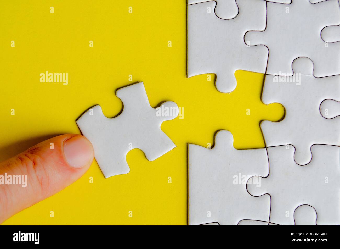 Top view of hand connecting a white jigsaw puzzle into its original ...