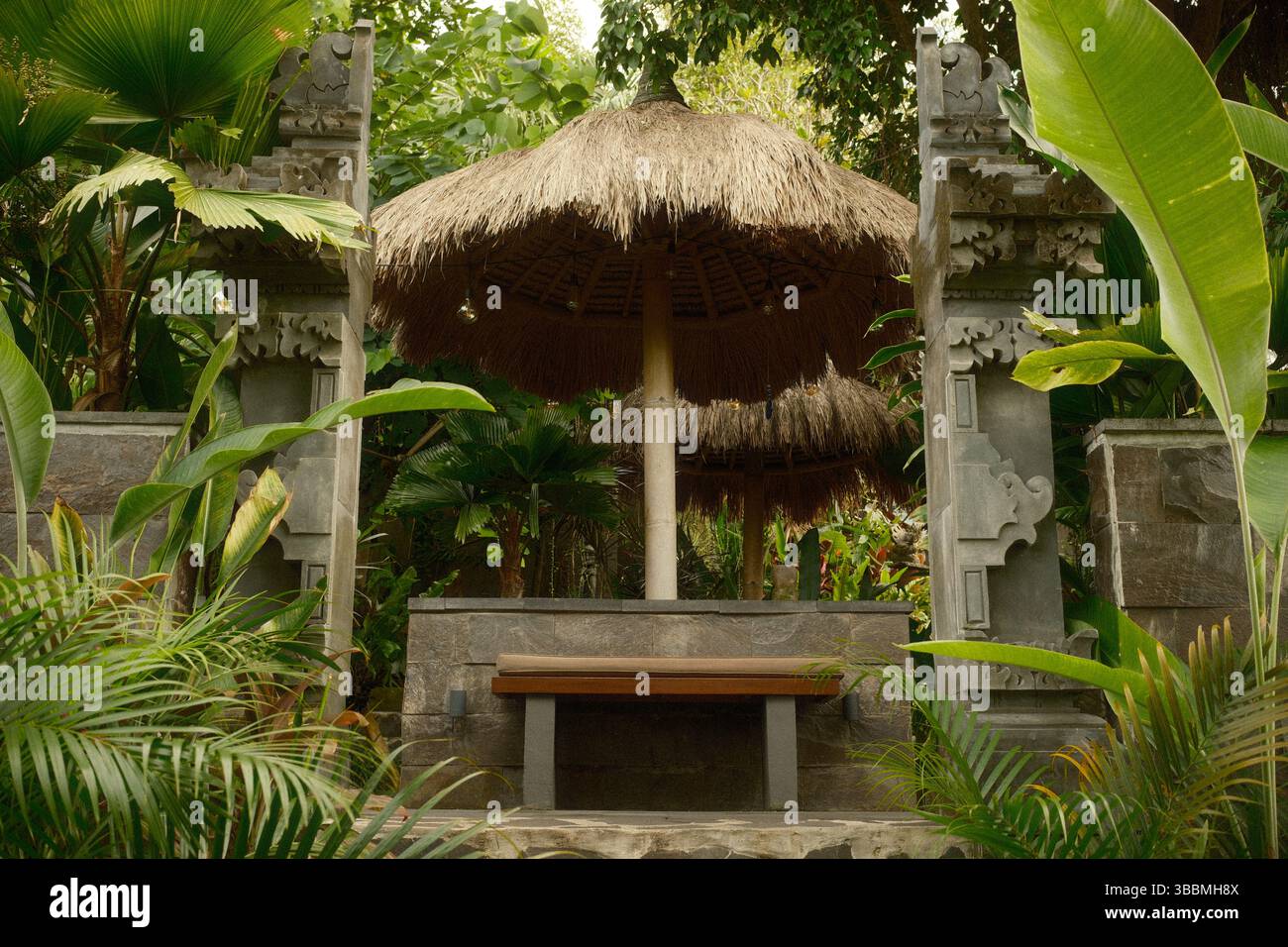 A traditional Balinese style resting bench with thatched roof and stone ...