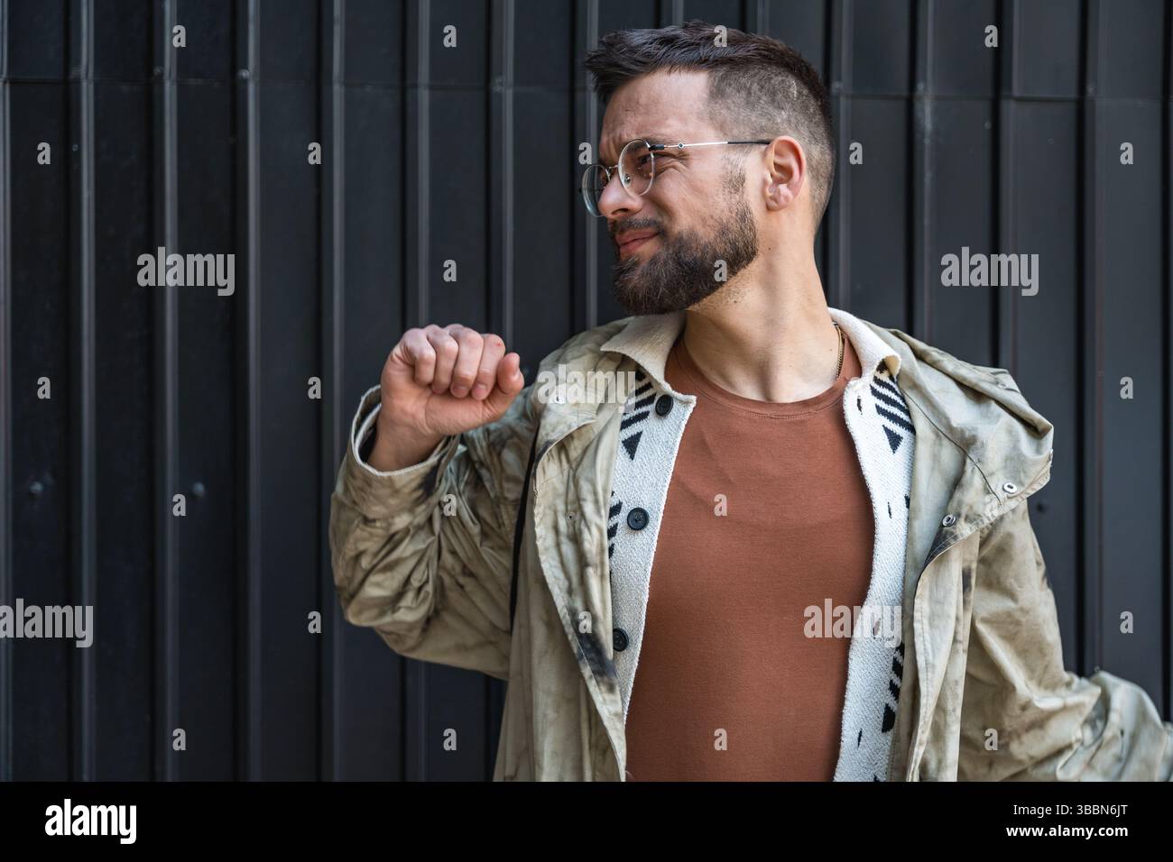 Portrait of young homeless man standing against black wall in the alley ...