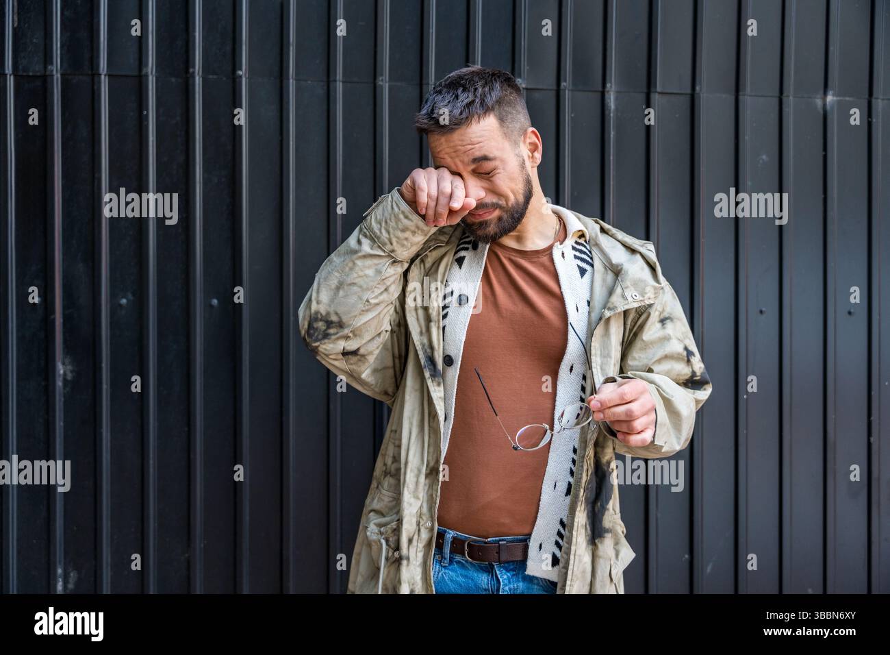 Portrait of young homeless man standing against black wall in the alley ...