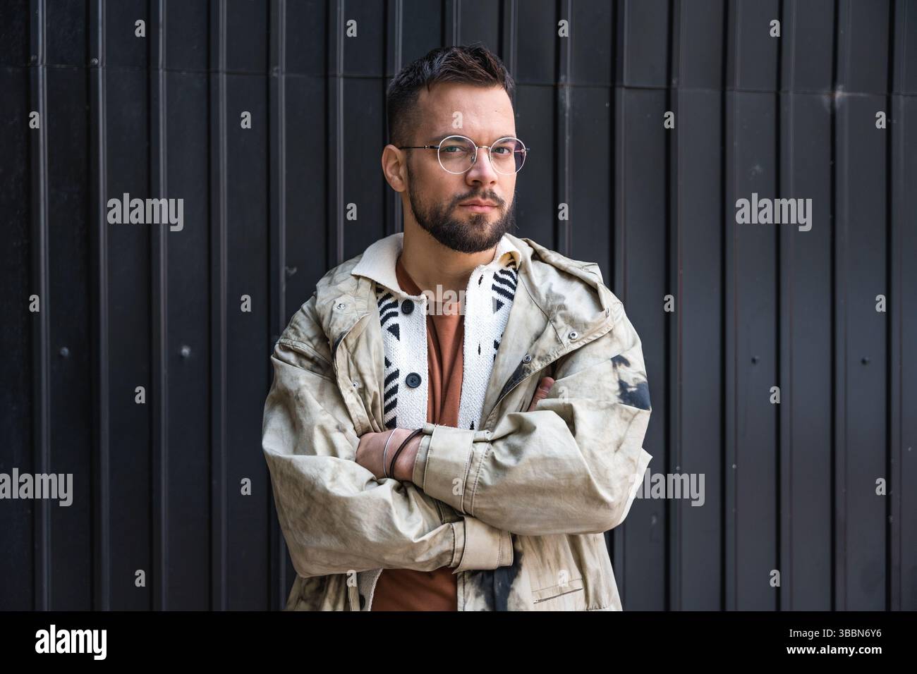 Portrait of young homeless man standing against black wall in the alley ...