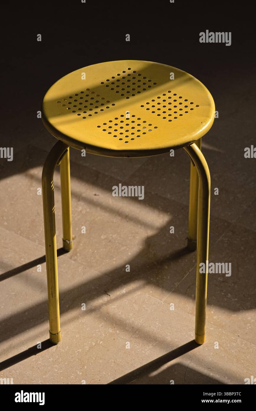 Yellow perforated metal stool in sunlight casting shadows on tiled ...