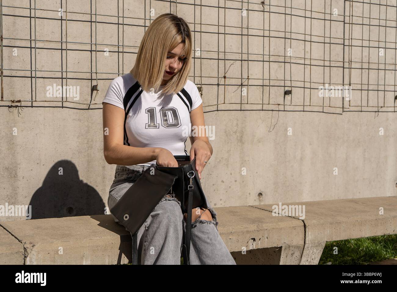 Young student opening her bag while sitting on a concrete bench in ...
