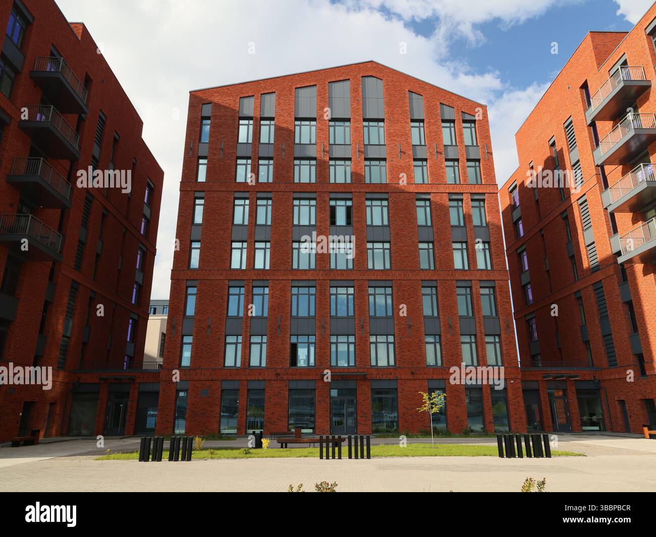 A modern residential complex featuring striking red brick and ample large windows throughout ...