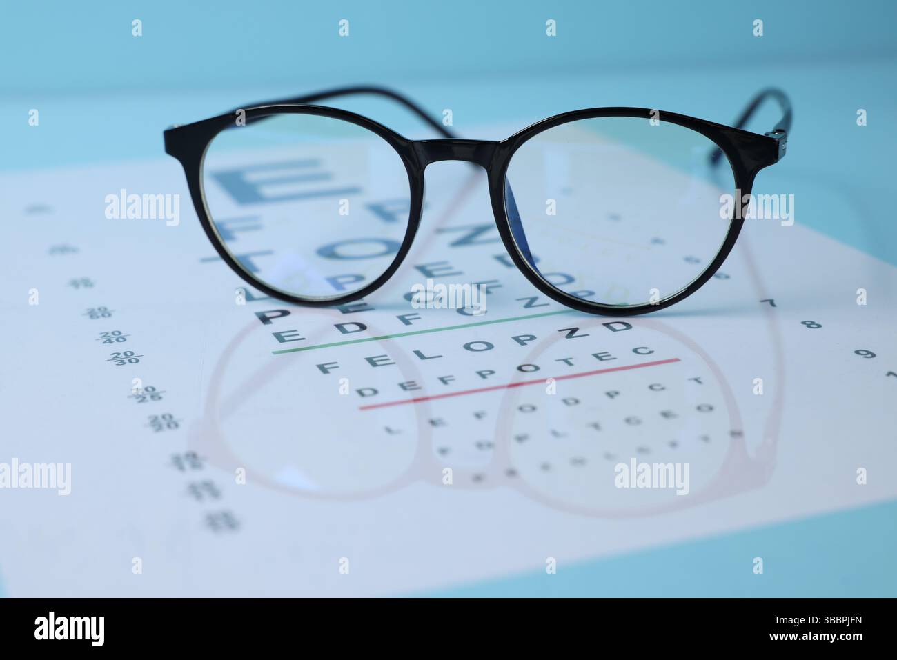 Glasses and vision test chart on light blue background, closeup Stock ...