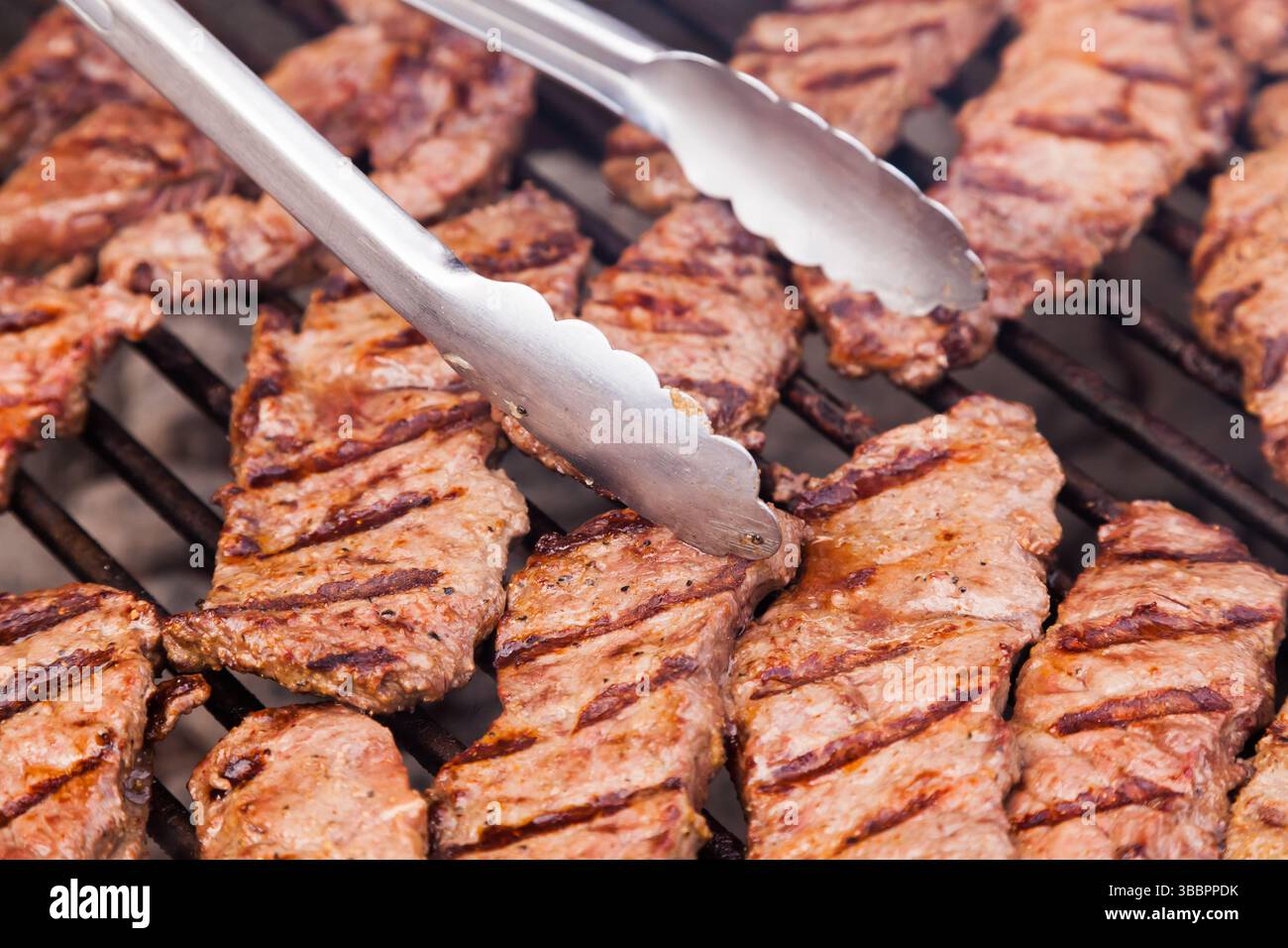 Beef meat with tongs to grip and turn the meat, grilled, close-up. Beef ...