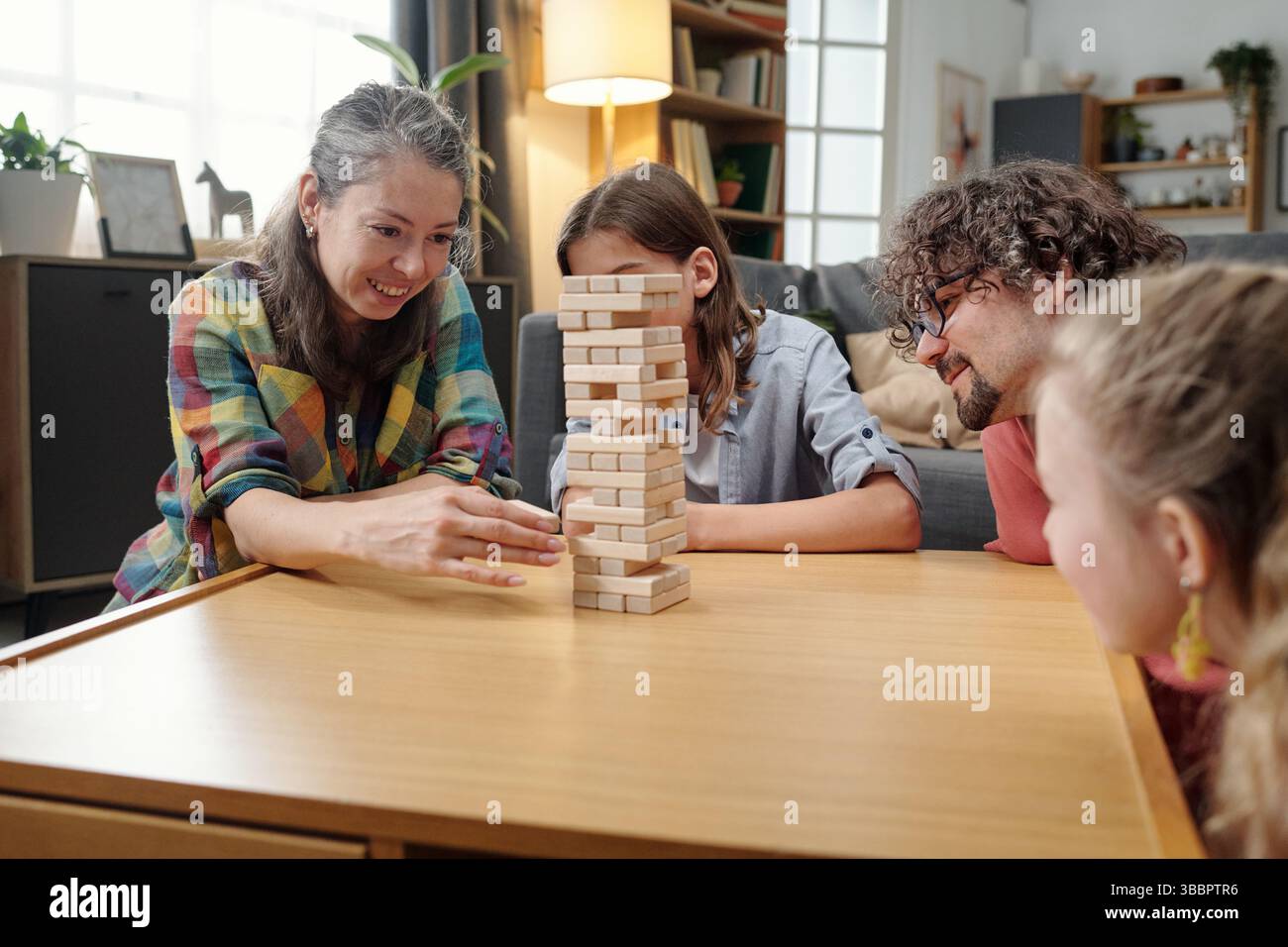 Happy family spending quality time together playing Jenga at home, engaging in fun activity ...