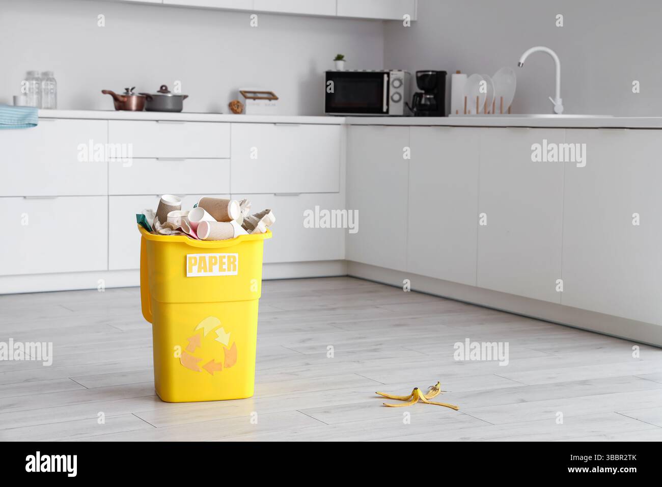 Full trash bin with PAPER sign and banana peel on floor in kitchen ...