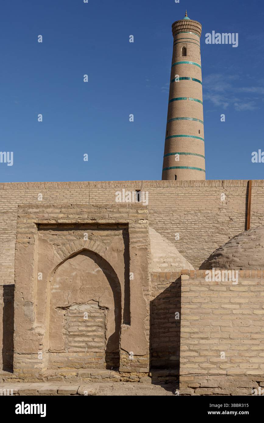 A tall minaret and large turquoise dome rise above sandy walls in the ...
