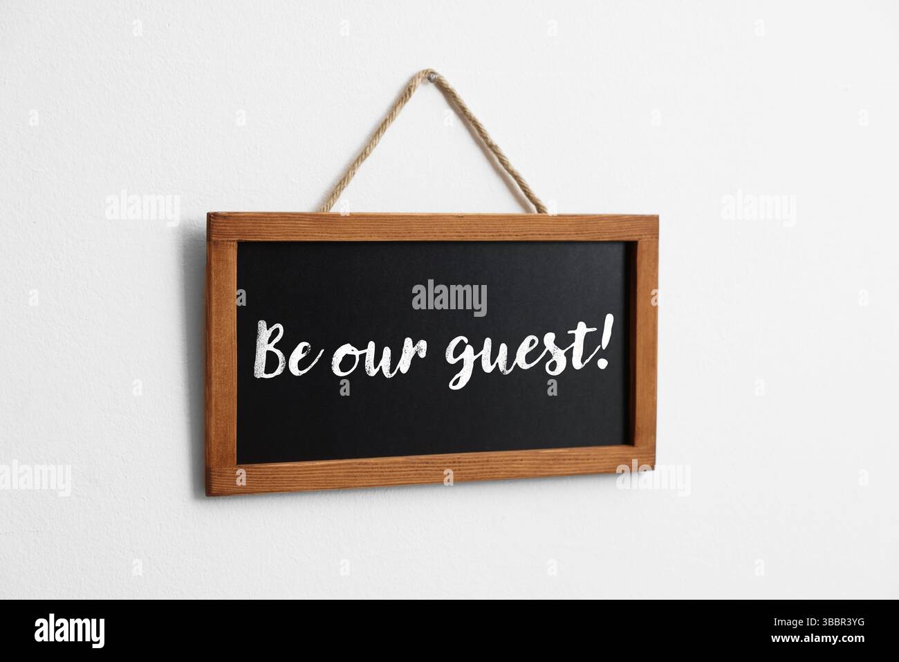 Small blackboard with phrase Be Our Guest hanging on white wall Stock ...