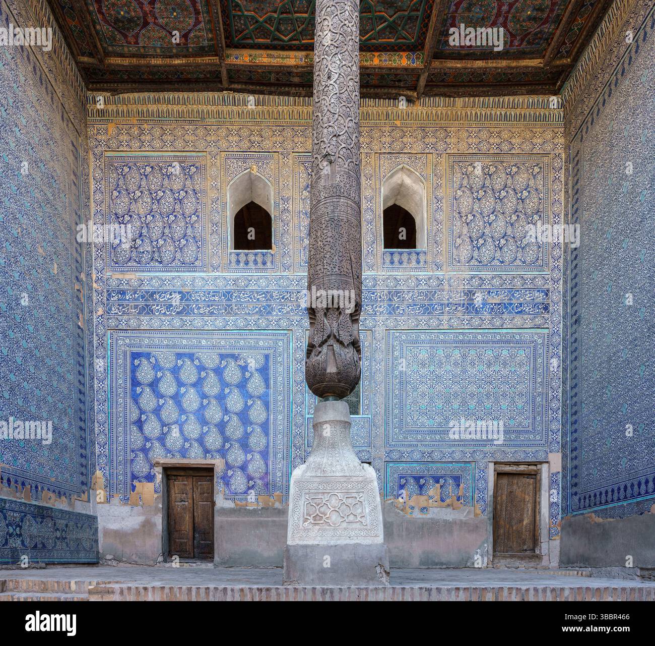 A carved wooden column rises from a blue tiled wall with geometric ...