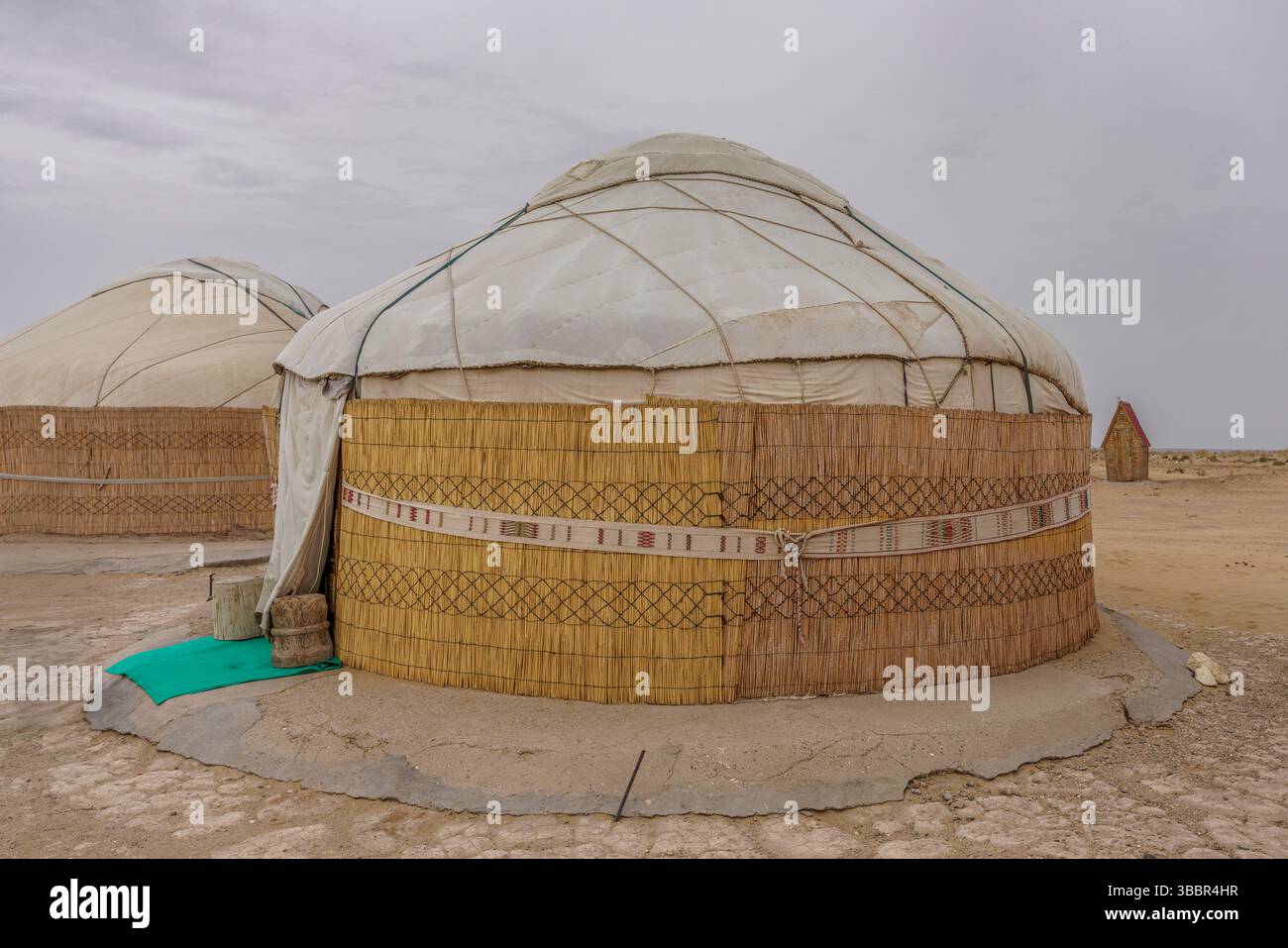 A traditional yurt with a rounded roof stands on sandy ground in ...