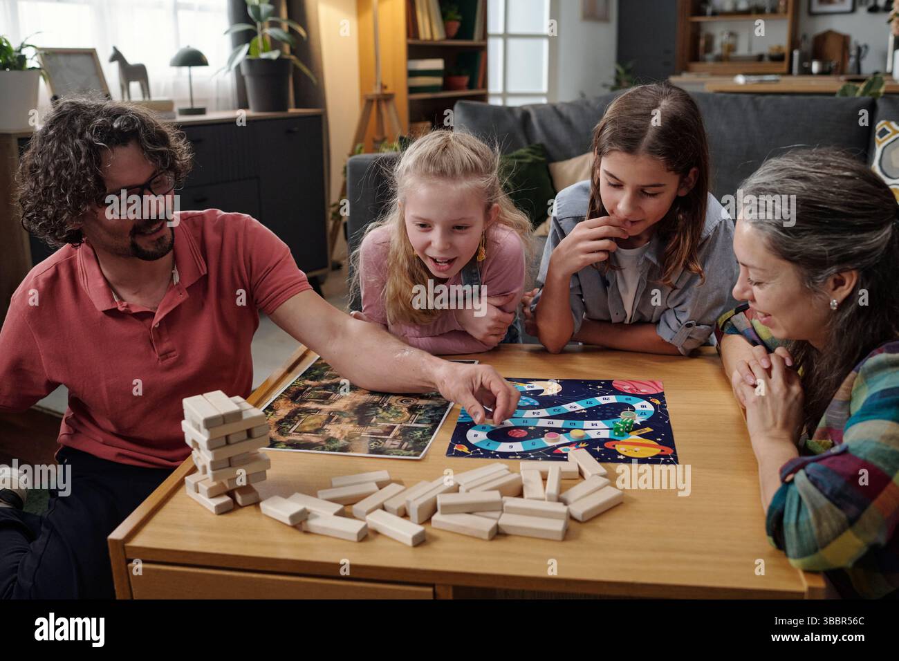 Family sitting at table playing board game, with three children and two ...