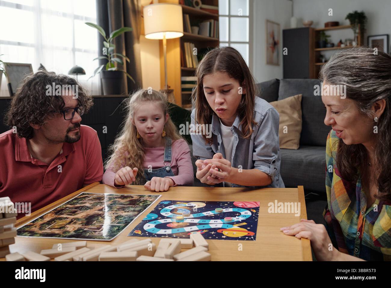 Family sitting around table in living room, playing board games ...