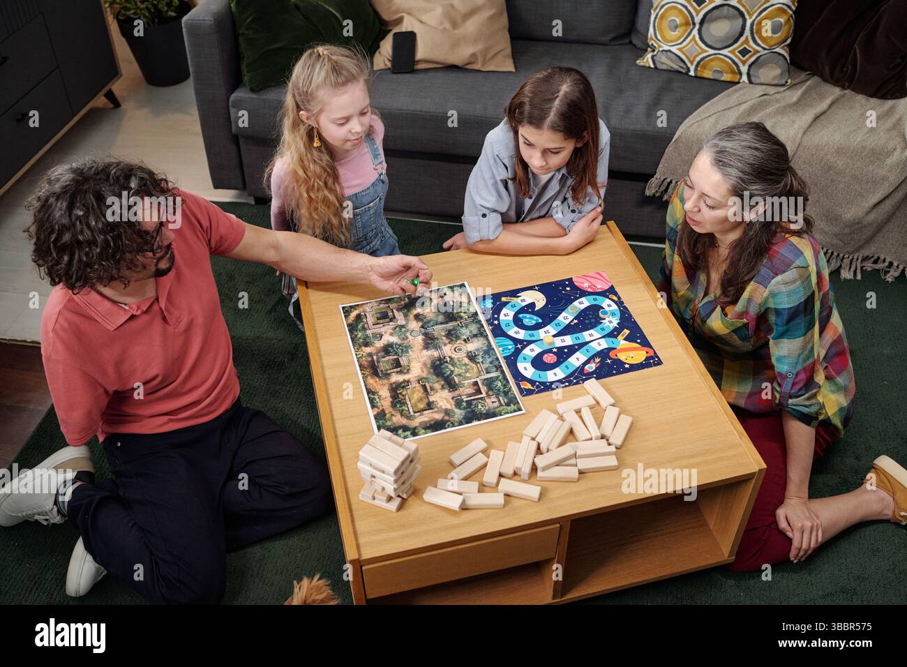 Family of four playing board game on wooden coffee table with variety ...
