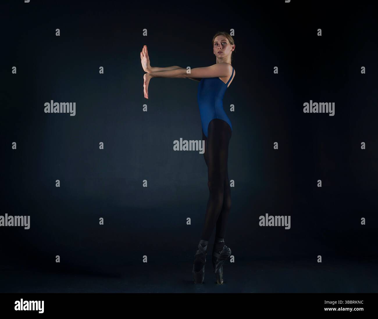 A ballerina in a blue leotard on a dark background shows ballet movements showing a stop gesture ...