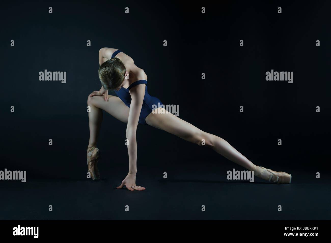 a ballerina on a dark background stands on pointe shoes demonstrating ballet movements and ...