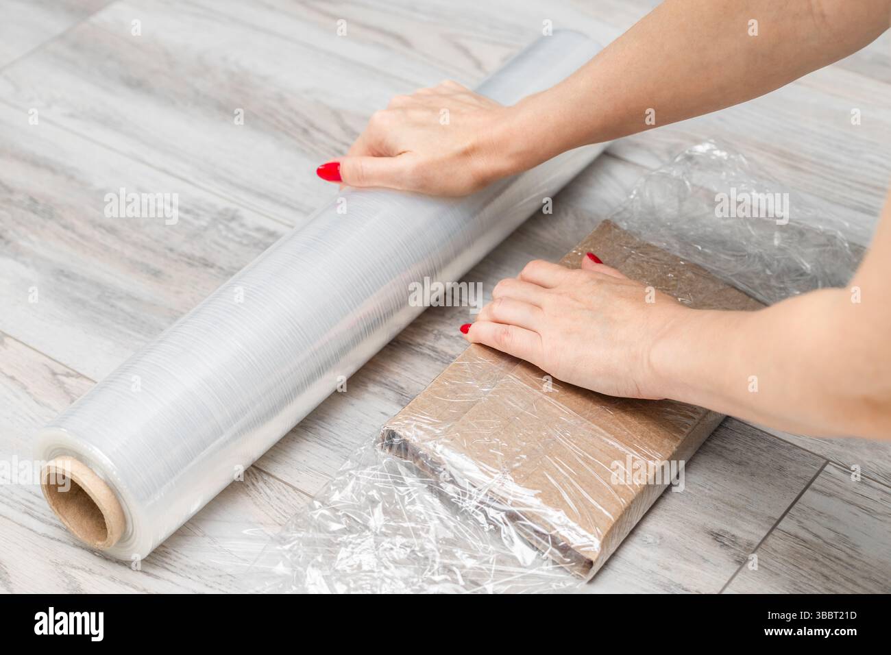 man wrapping cardboard box with transparent stretch film. woman packing ...