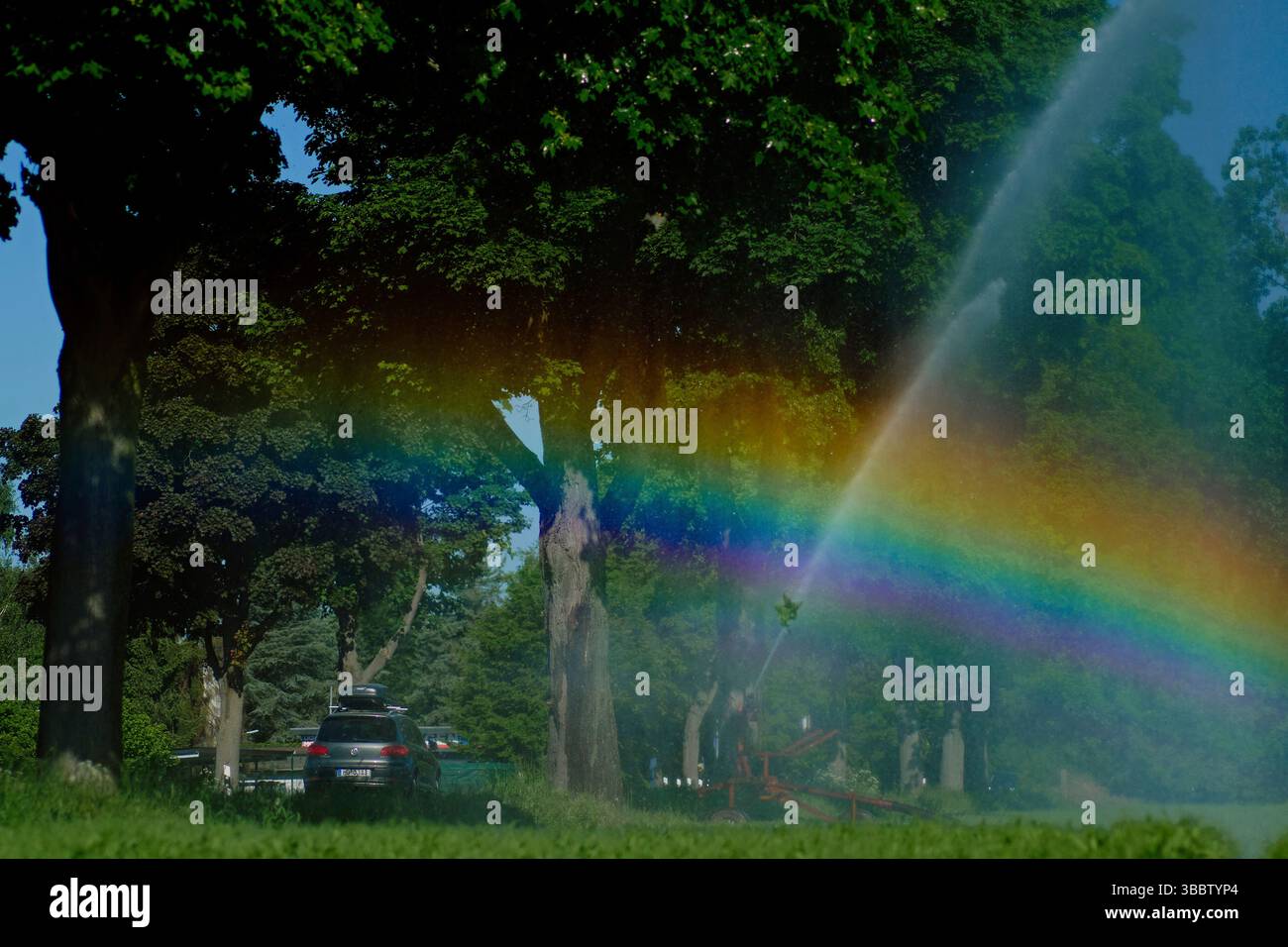 A sprinkler system standing in a field creates a rainbow in the ...