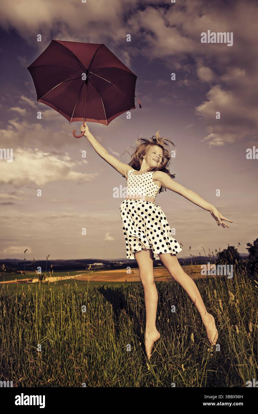 Teen girl jumping with an umbrella in front of rural landscape Stock ...