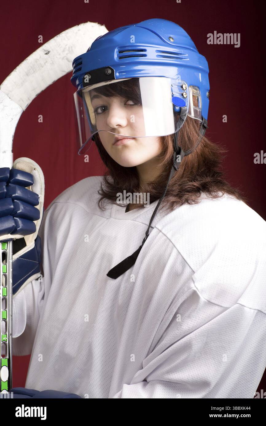 A girl hockey player in uniform posing with helmets off in front of red ...