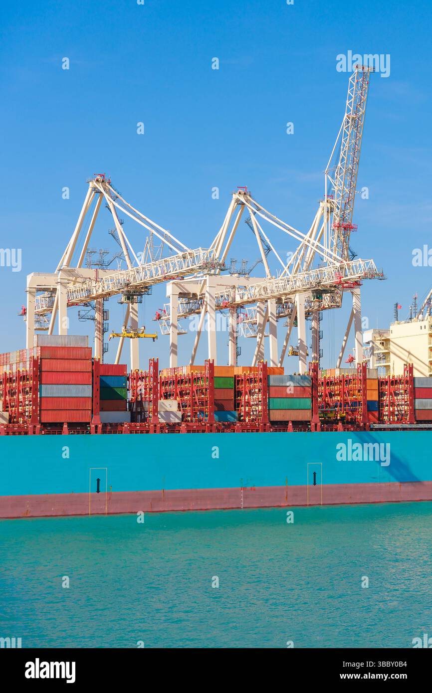 A massive cargo ship sits at a busy port. Cranes tower above the ...