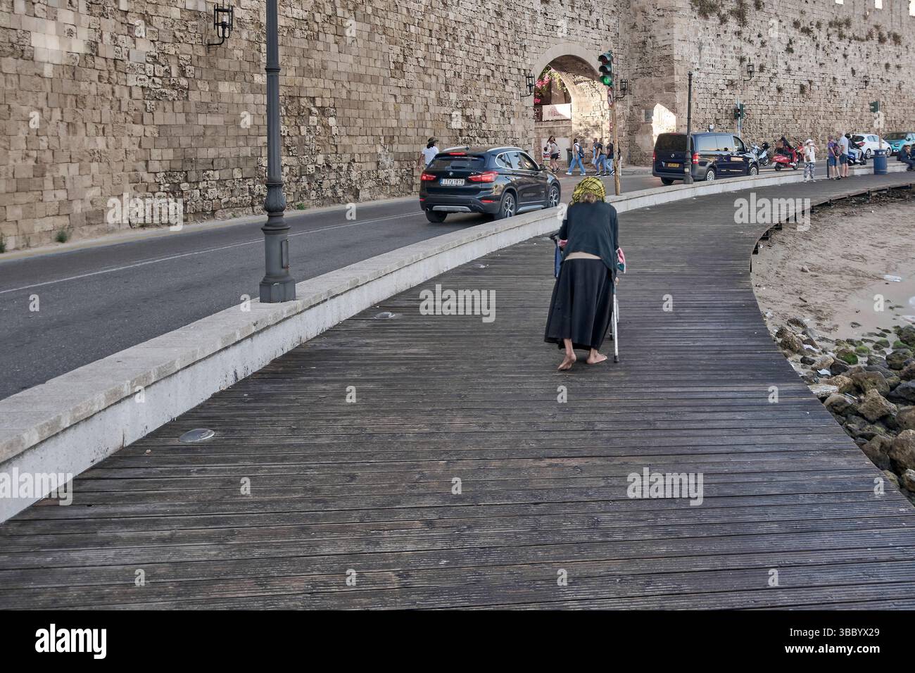Crete.Greece - may 17, 2025: A barefoot elderly woman walks with a cart ...