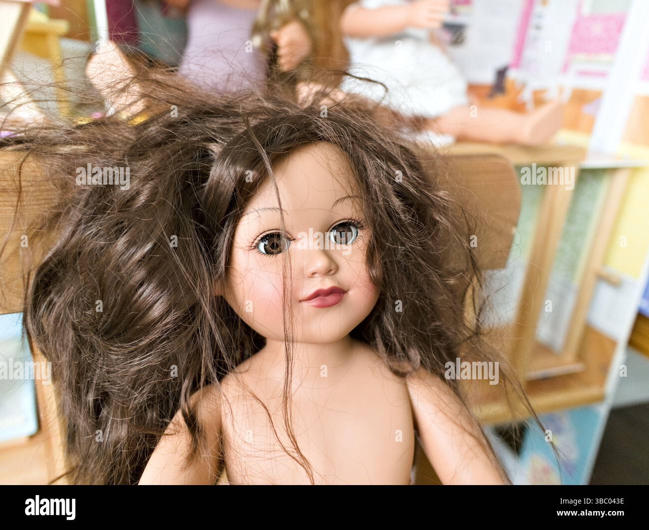 A doll with long brown hair is sitting on a chair. The hair is messy ...