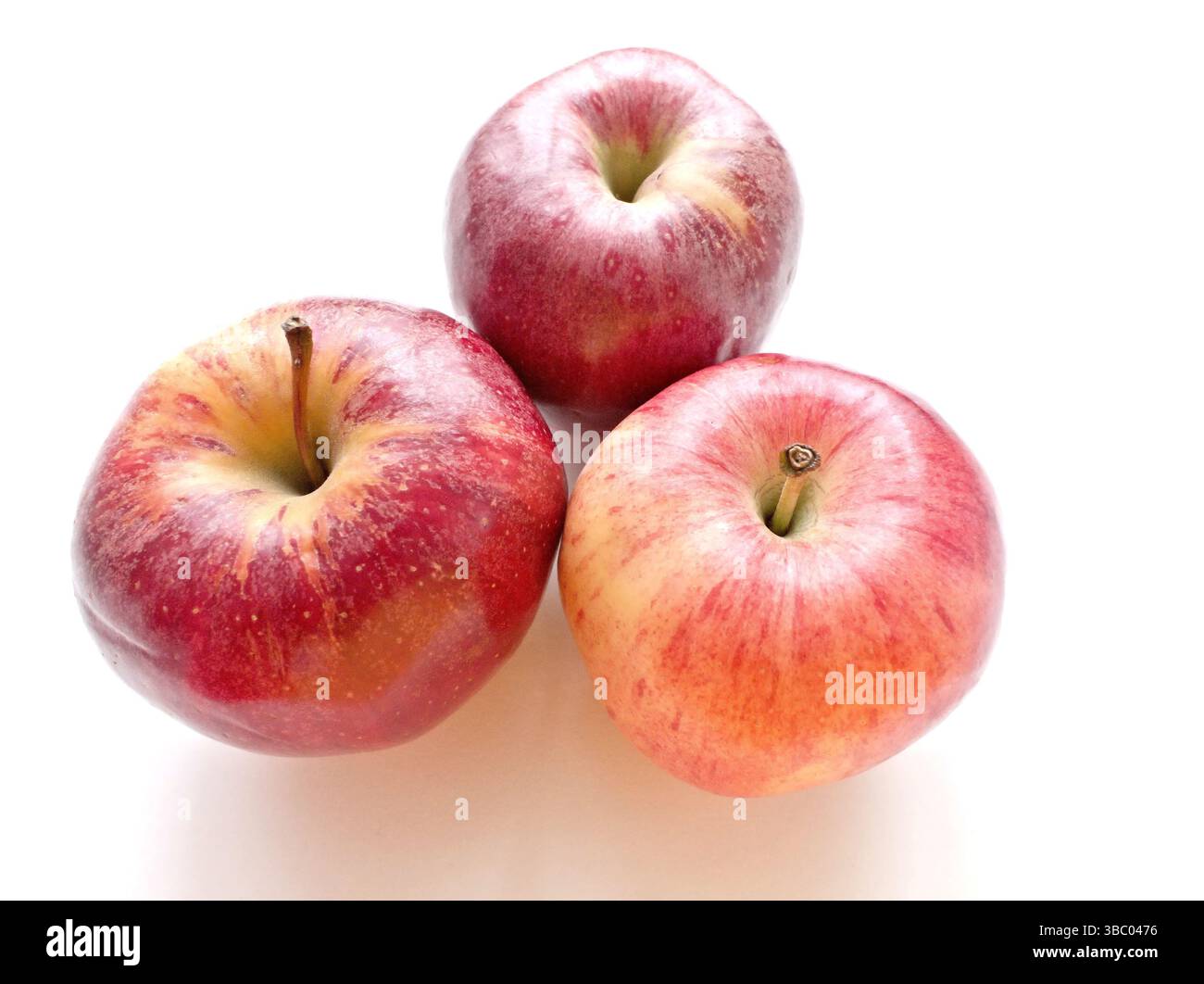 Three apples are sitting on a white surface. They are red and shiny ...
