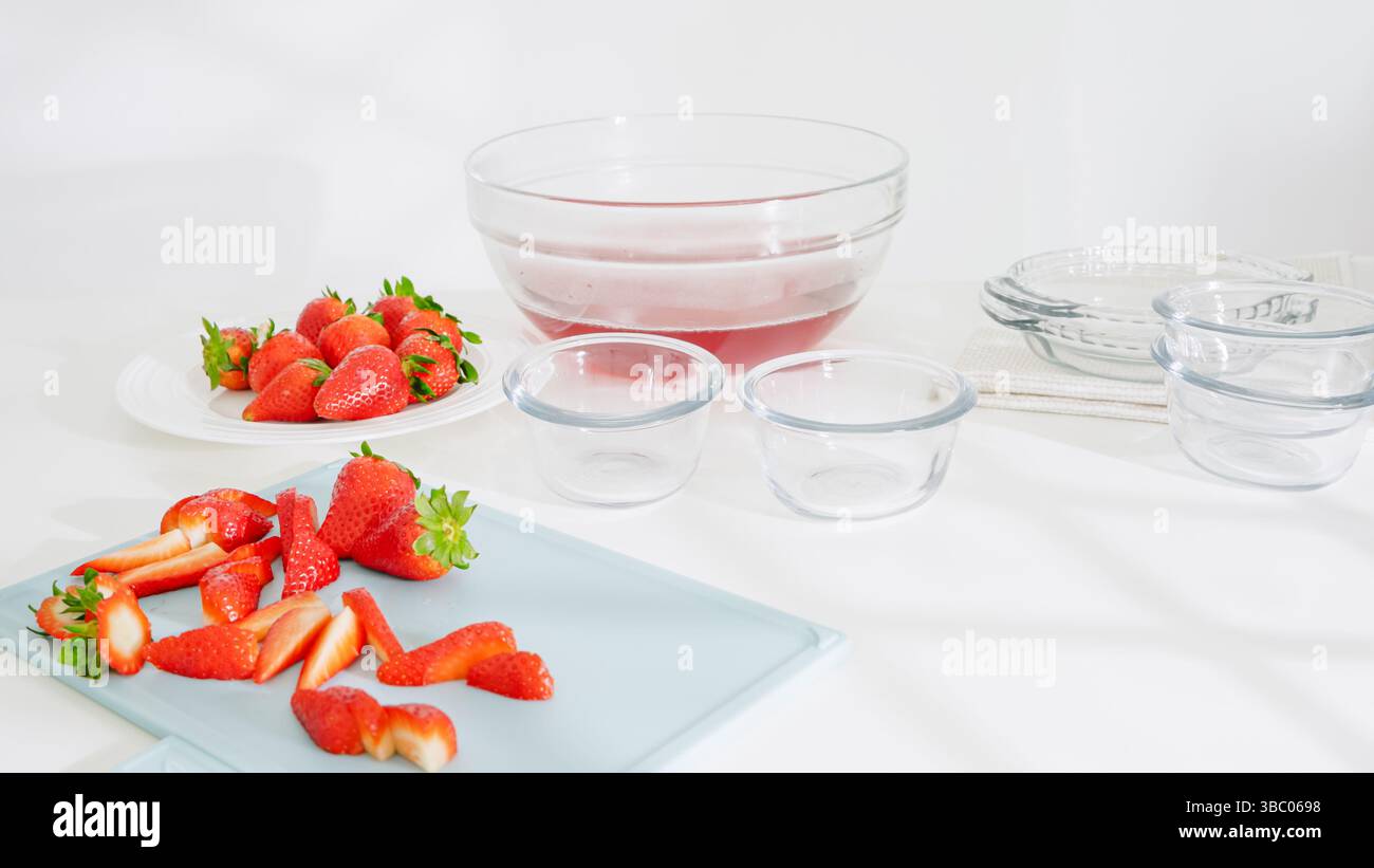 Glass bowls and a large mixing bowl with strawberry jelly base on a ...
