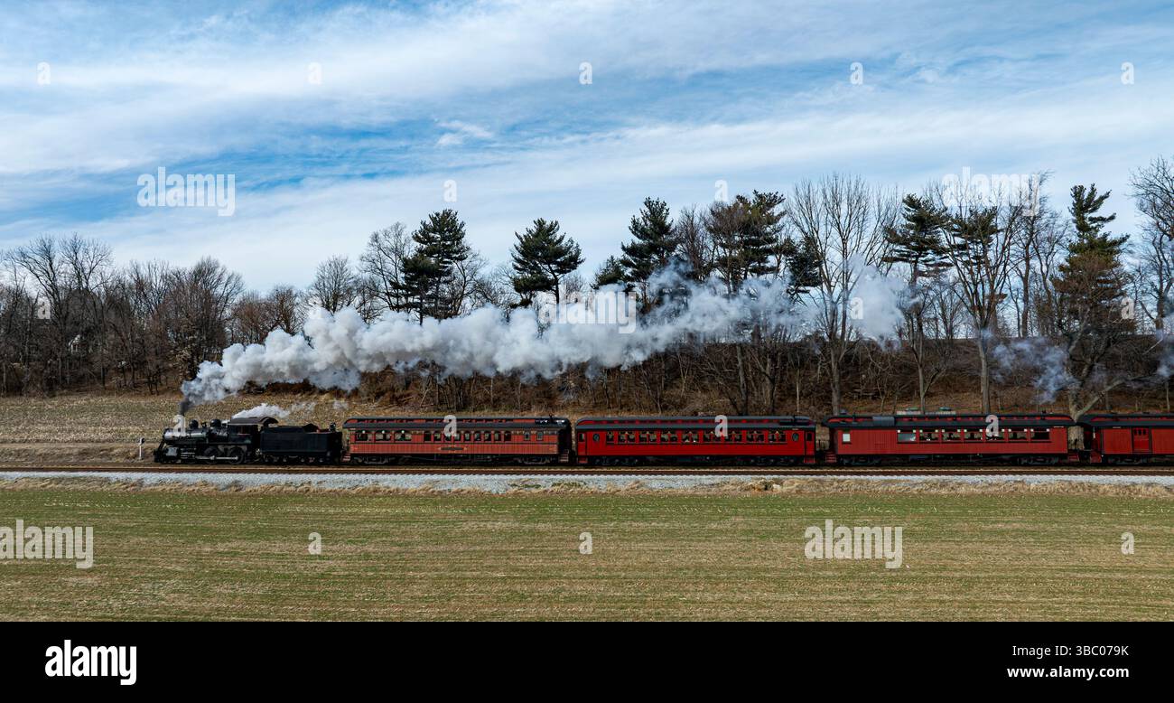 A vintage steam train chugs along a rural landscape, with rolling ...