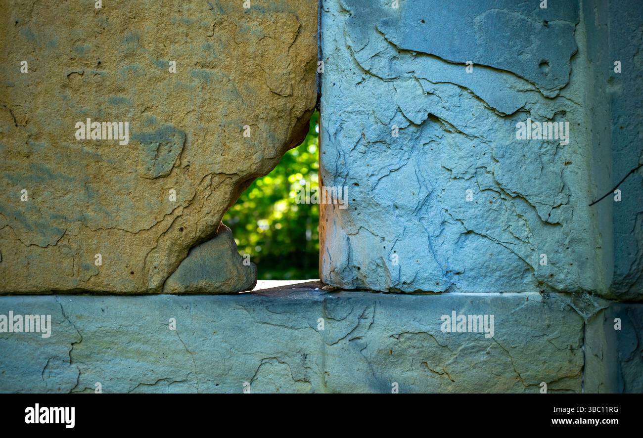 Close-up of a weathered stone wall with a narrow gap revealing lush ...
